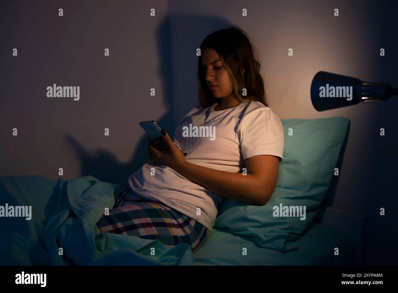 Portrait of beautiful teen girl lying on bed and typing message on ...