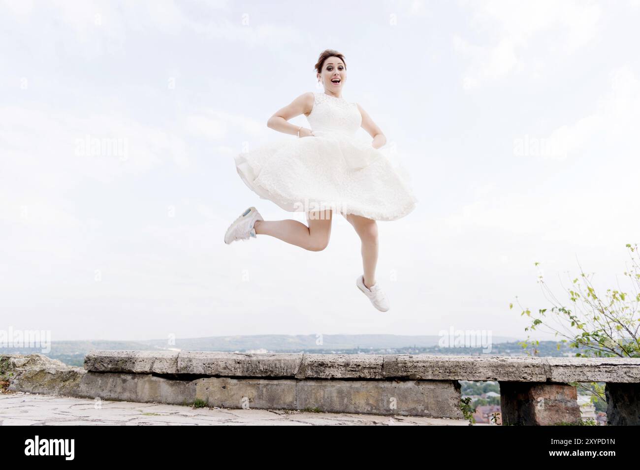 The crazy bride jumps and hangs in the sky against the backdrop of the cityscape of a small ...