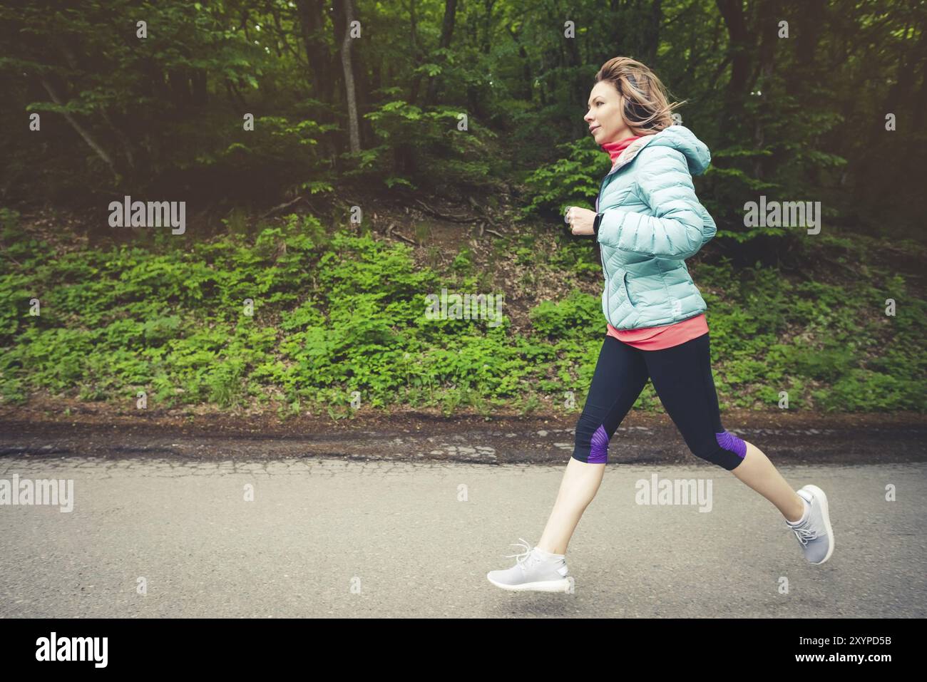 A young blonde woman running is practicing outdoors in a city mountain ...
