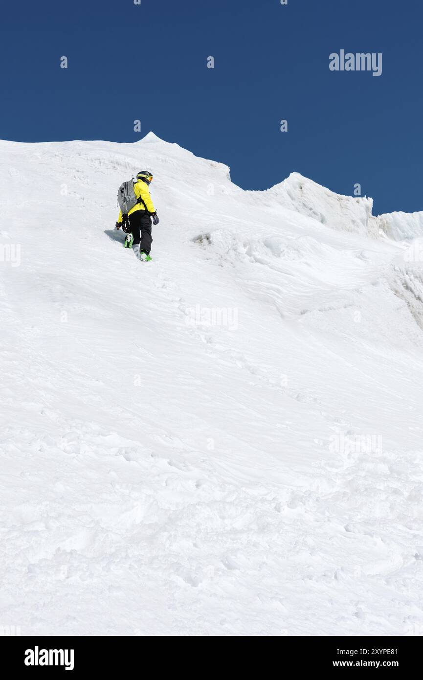 A skier in a helmet and mask with a backpack rises on a slope against ...