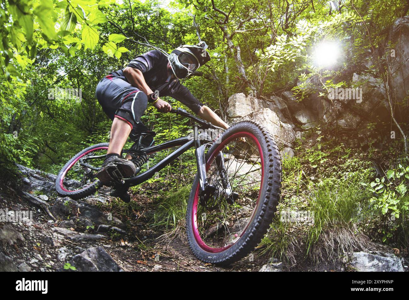 A young rider on a bicycle for downhill descends the rocks in the ...