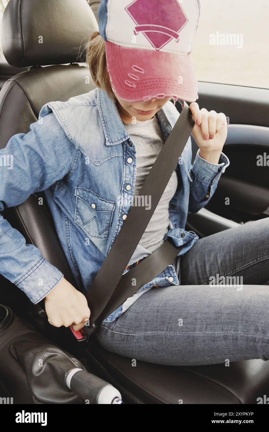 A hipster girl wearing jeans clothes fastens her seat belt in the car ...