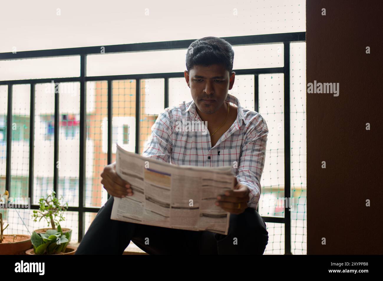 The young man sits comfortably on a balcony, focused intently on ...
