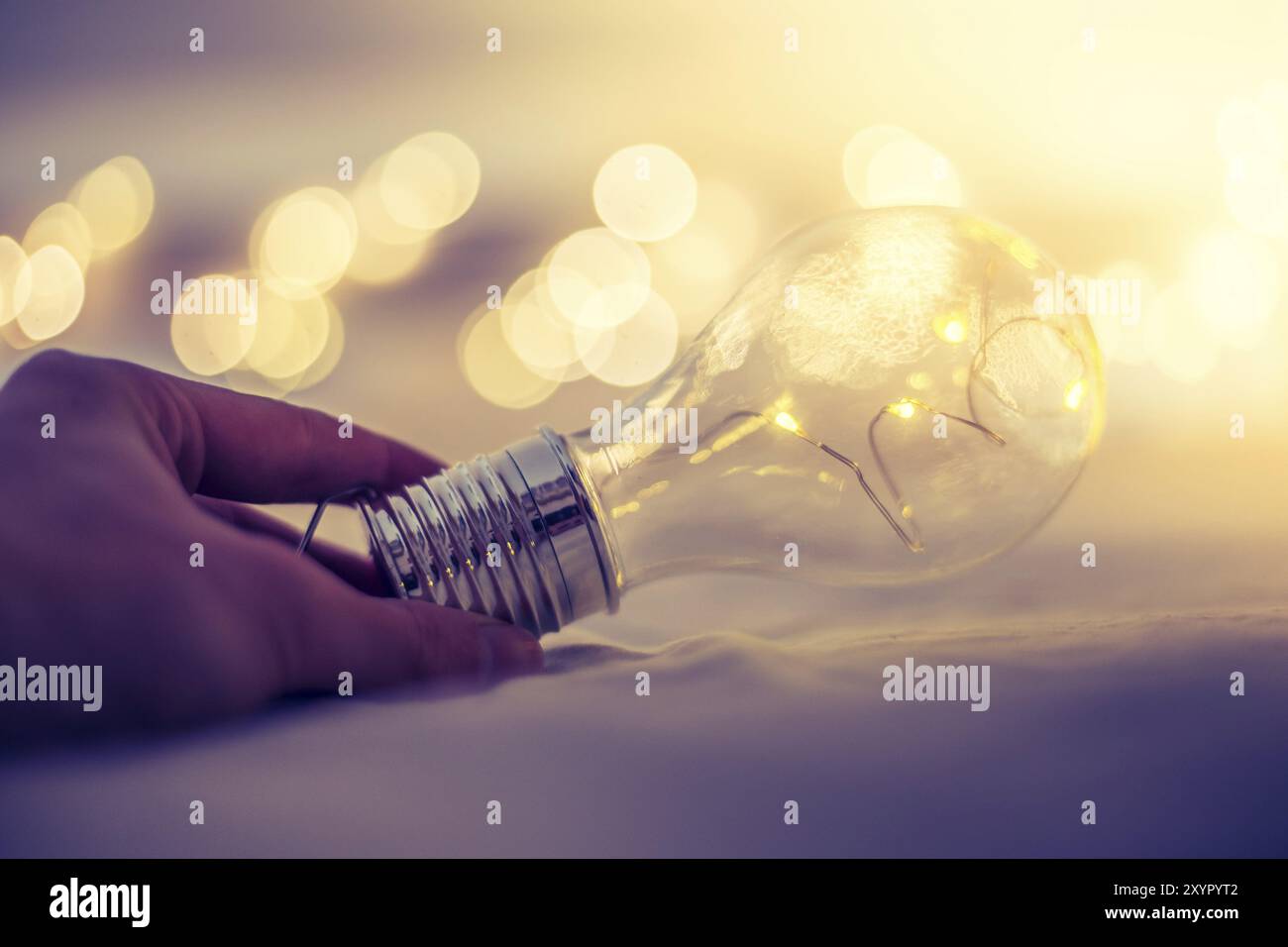 LED light bulb is lying in the bed, hands touching. Symbol for ideas ...