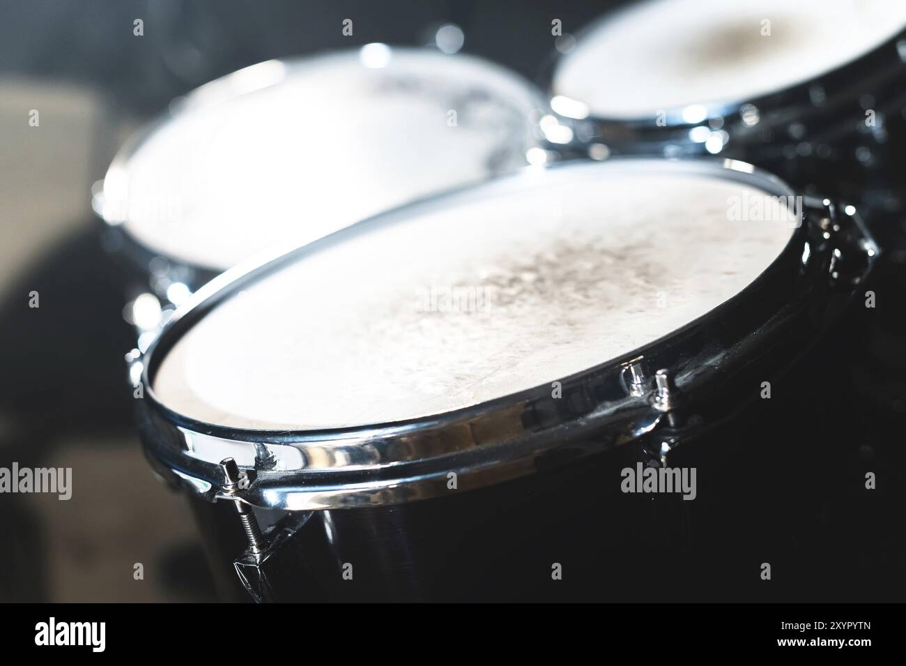 Closeup view of a drum set in a dark studio. Black drum barrels with ...