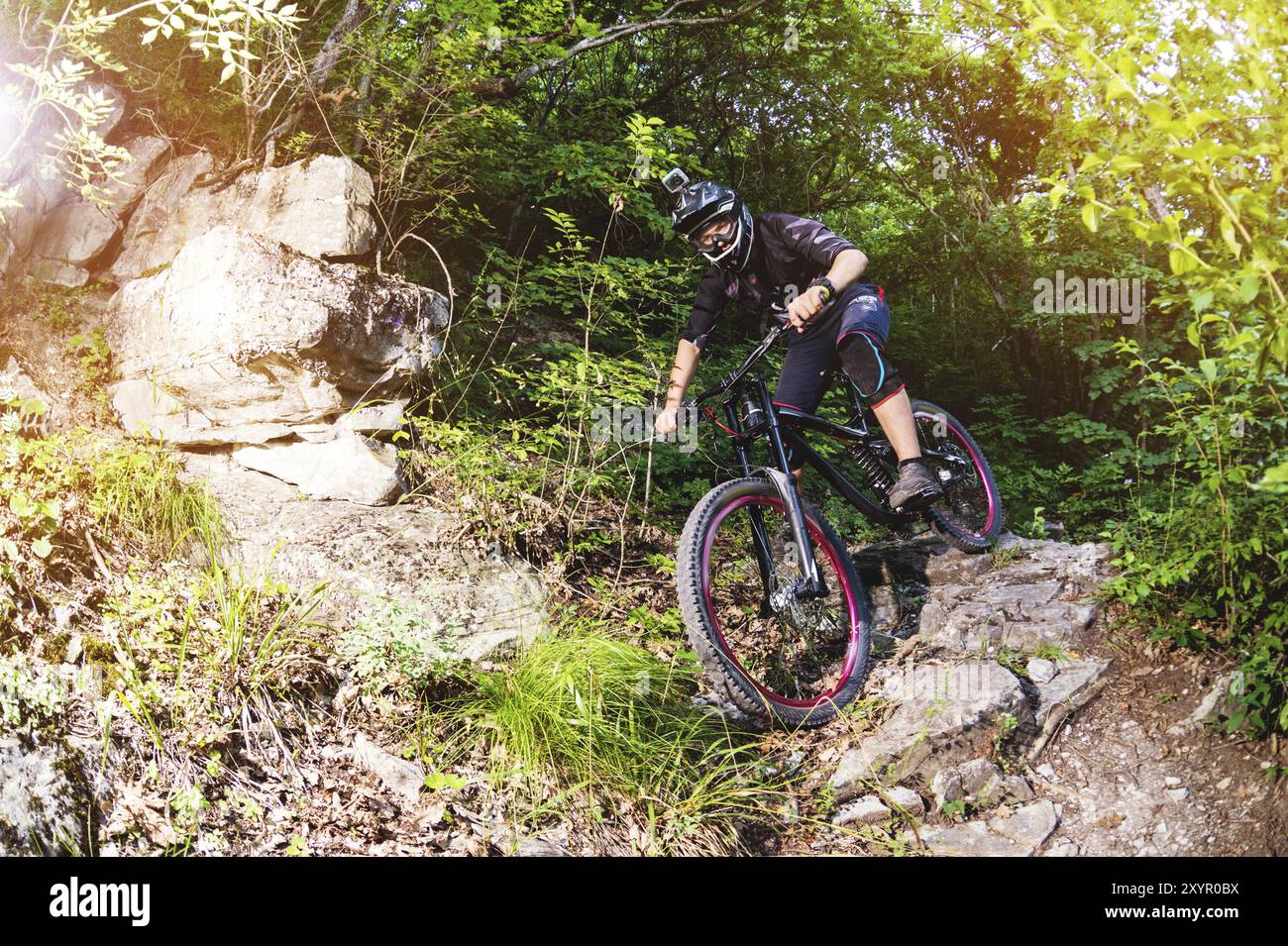A young rider on a bicycle for downhill descends the rocks in the ...