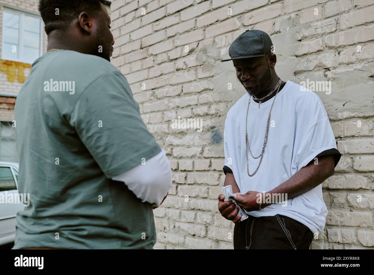 Man leaning on old garage wall while counting money, customer waiting ...