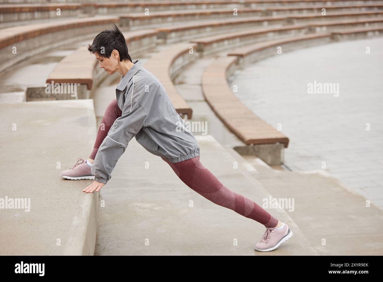 Side view of fit senior woman in pink sportswear stretching leg muscles ...