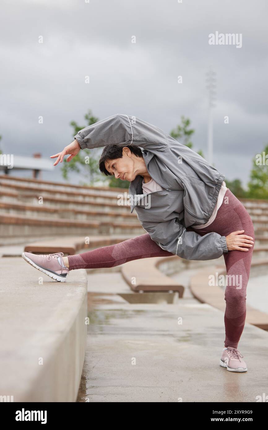 Side view of elderly woman in pink leggings stretching muscles reaching ...