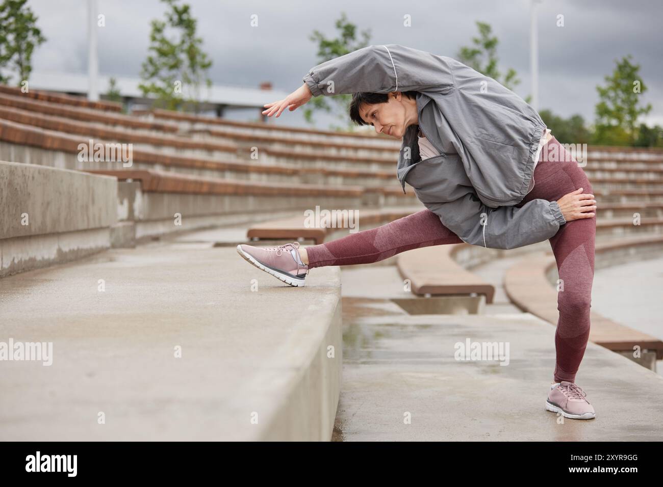 Side view of elderly woman in pink leggings stretching back muscles ...