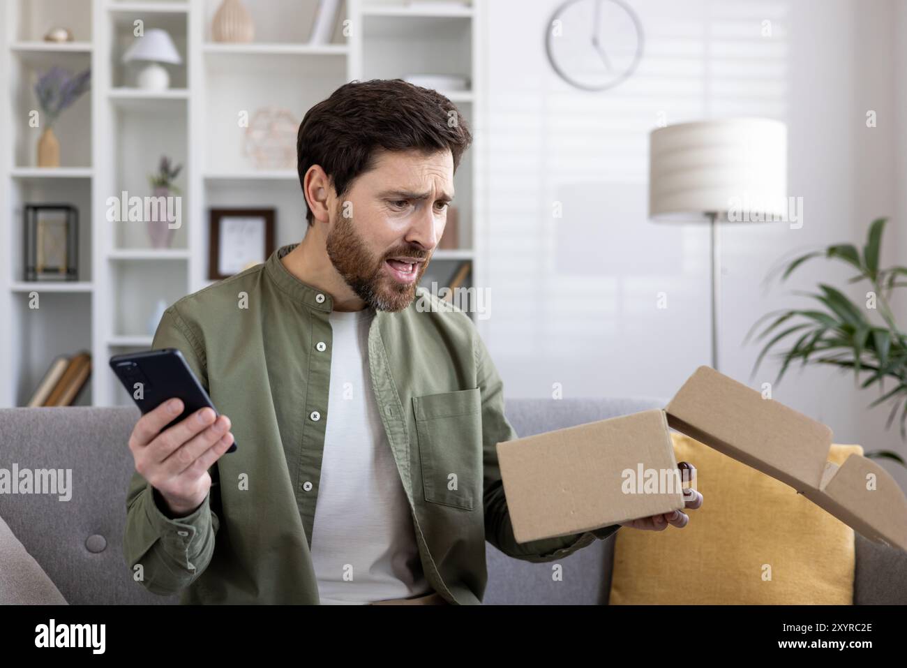 Frustrated man sitting on couch holding smartphone and empty box ...