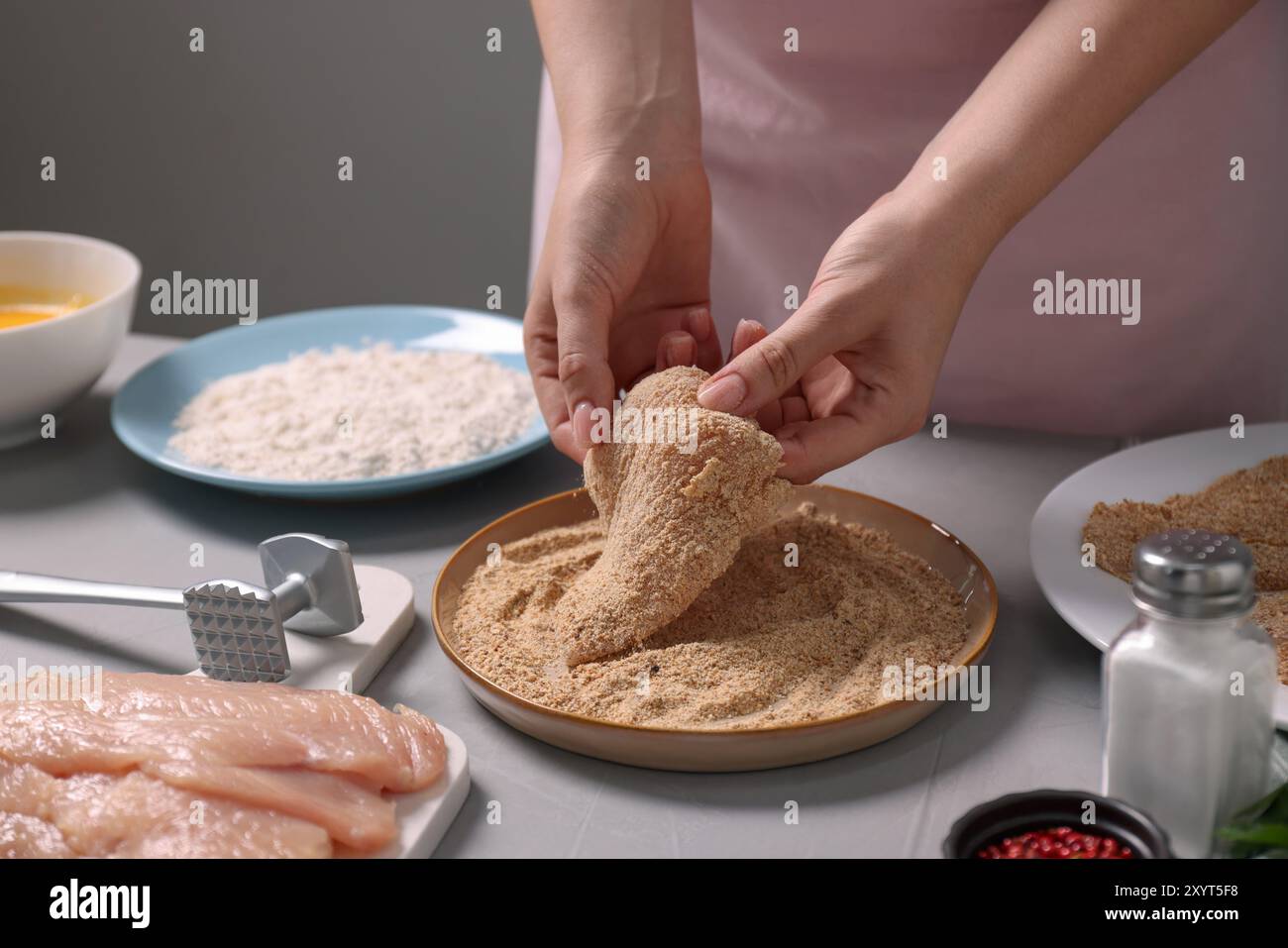 Making schnitzel. Woman coating slice of meat with bread crumbs at grey ...