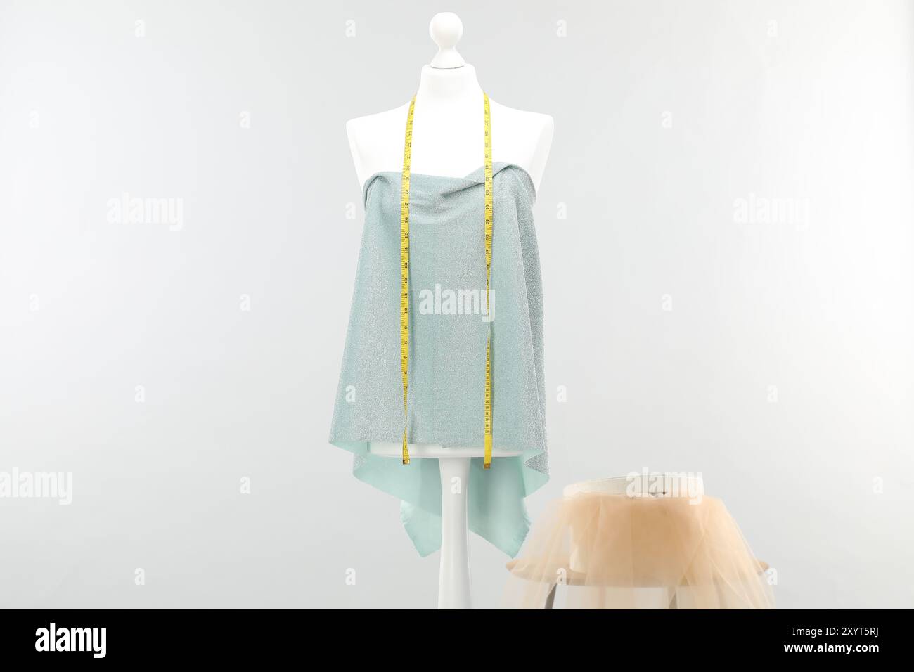 Mannequin with measuring tape, fabric and box on side table against ...