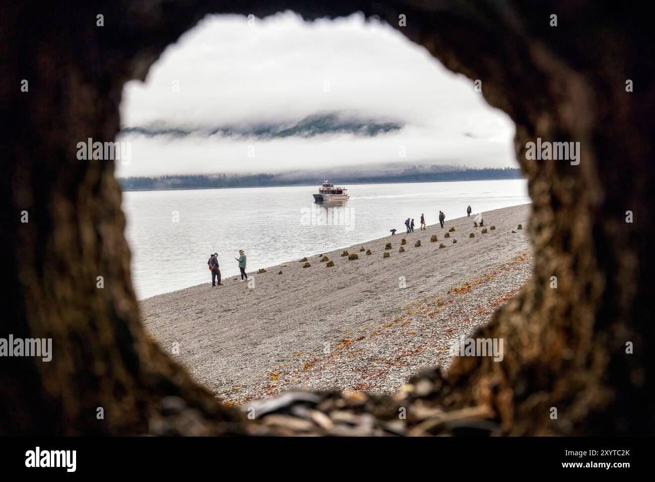 Tourists on the beach at Icy Strait Point framed through a wooden hole ...