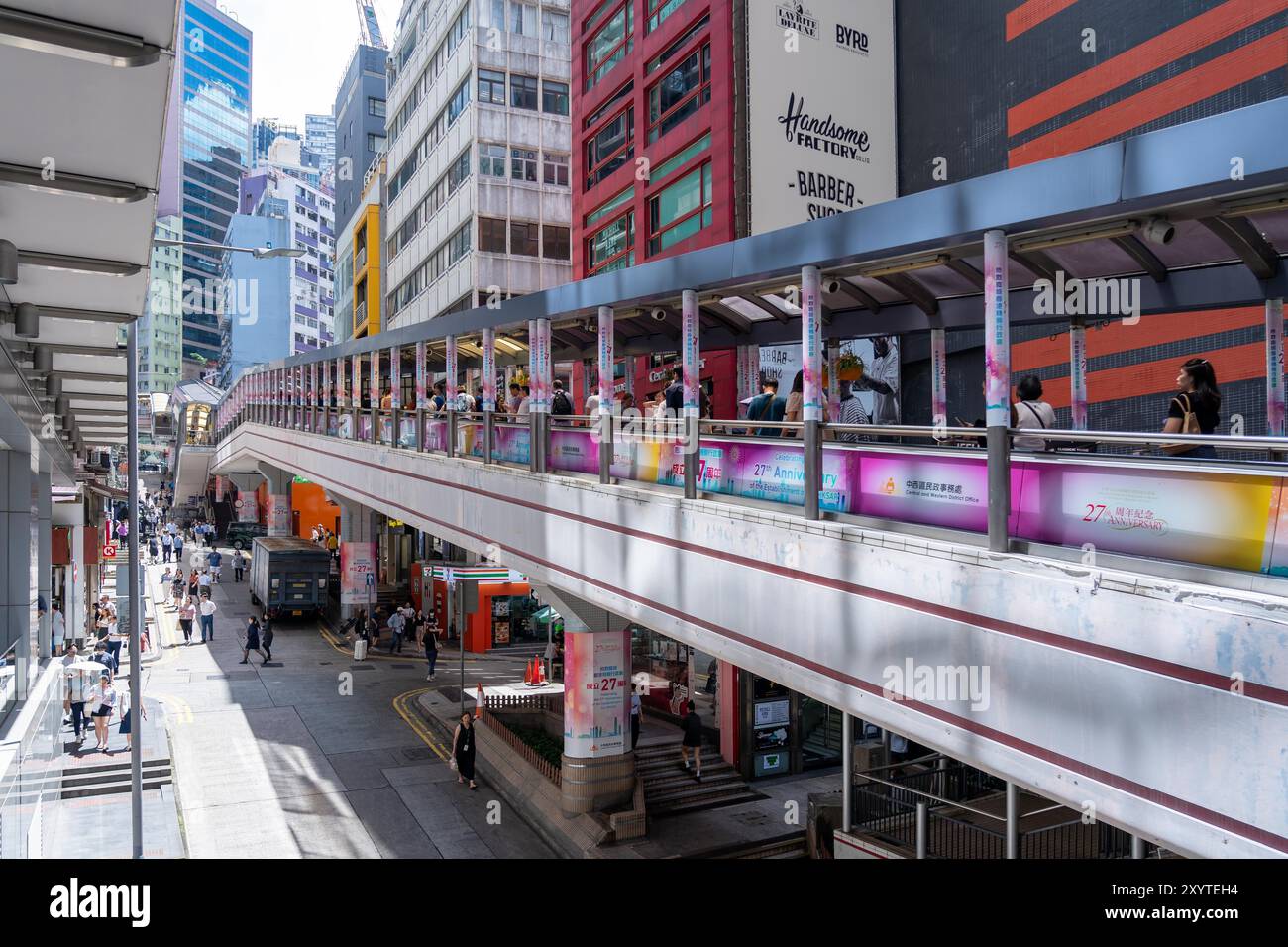 Hong Kong, China - July 03, 2024 : A pedestrian walkway bridges above a busy city street in Hong ...