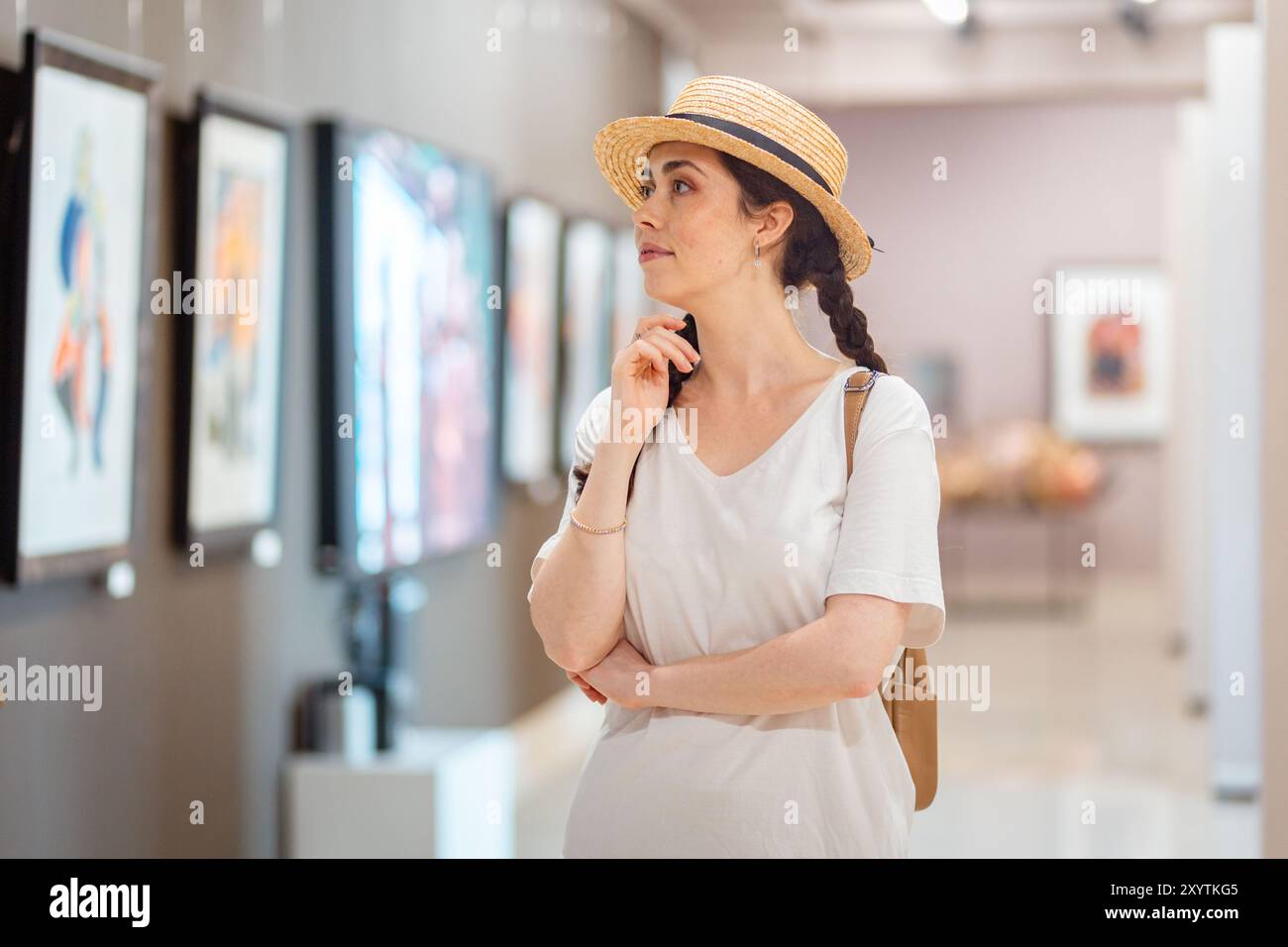Historic education. Pretty young Caucasian woman wearing straw hat admiring paintings in the ...