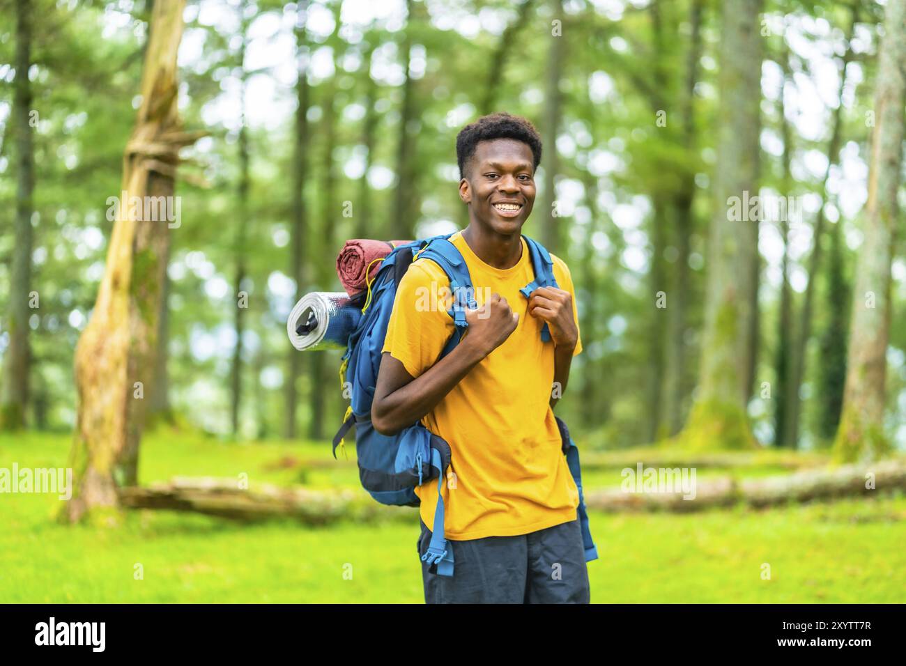 Portrait of a cheerful young african man hiking through green forest ...