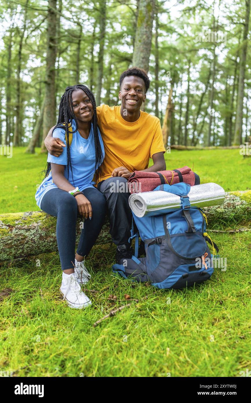 Vertical portrait of young african friends embracing sitting on a log ...