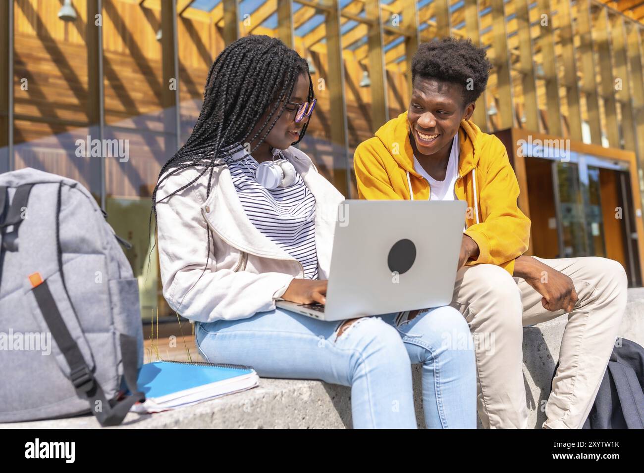 Two young male and female african students smiling while using laptop ...