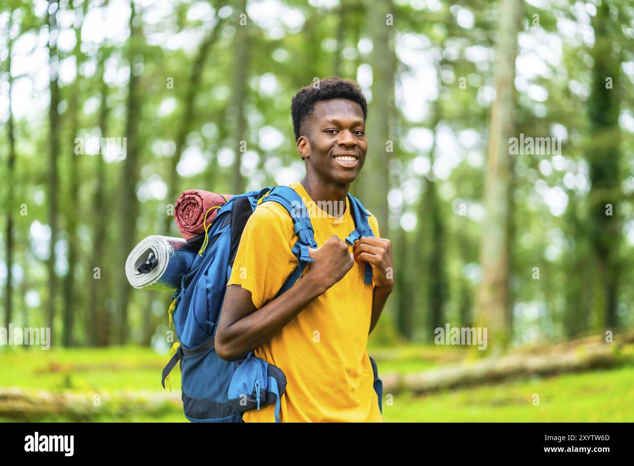 African young man carrying rucksack smiling at camera while hiking the ...