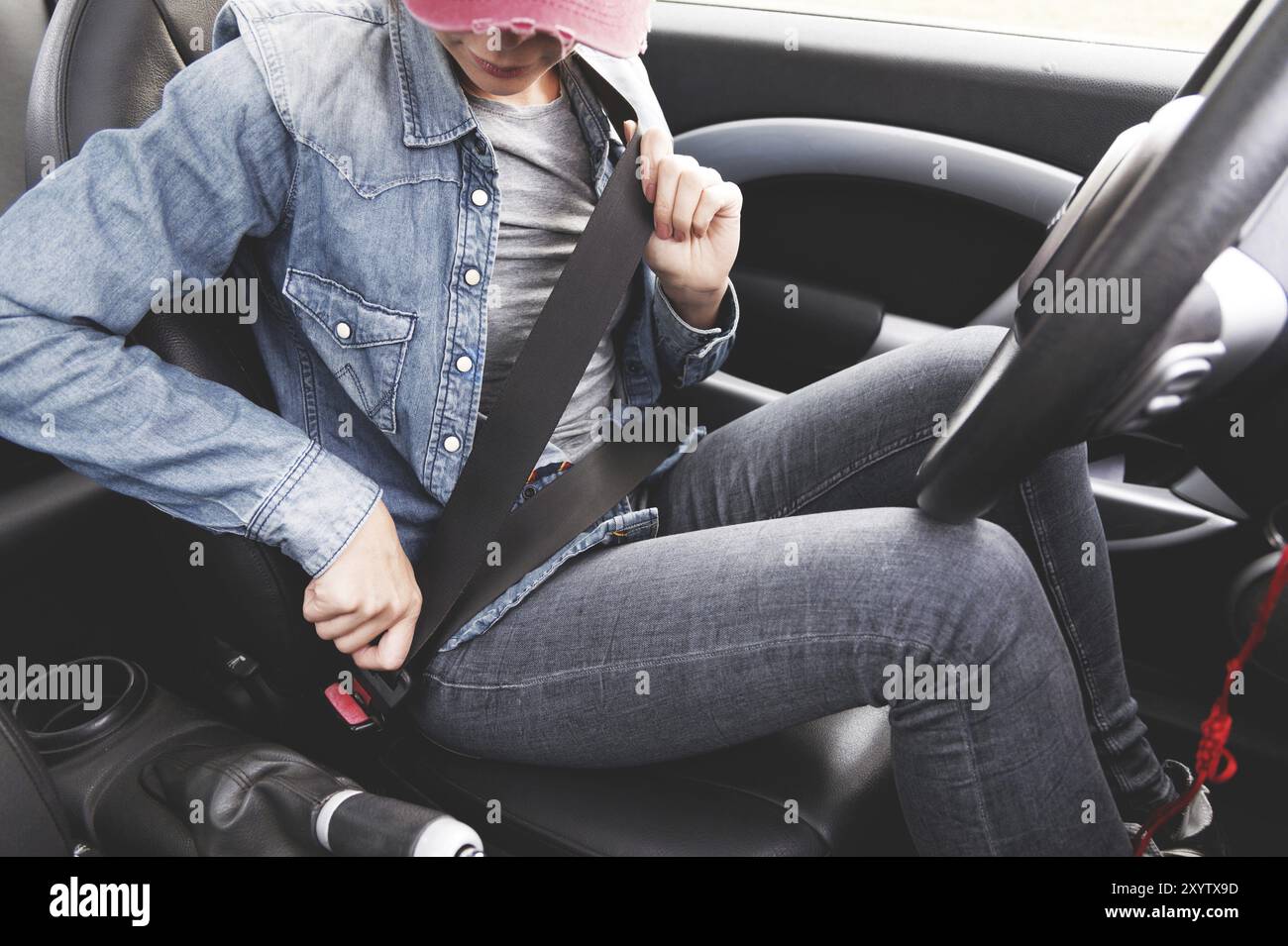 A hipster girl wearing jeans clothes fastens her seat belt in the car ...