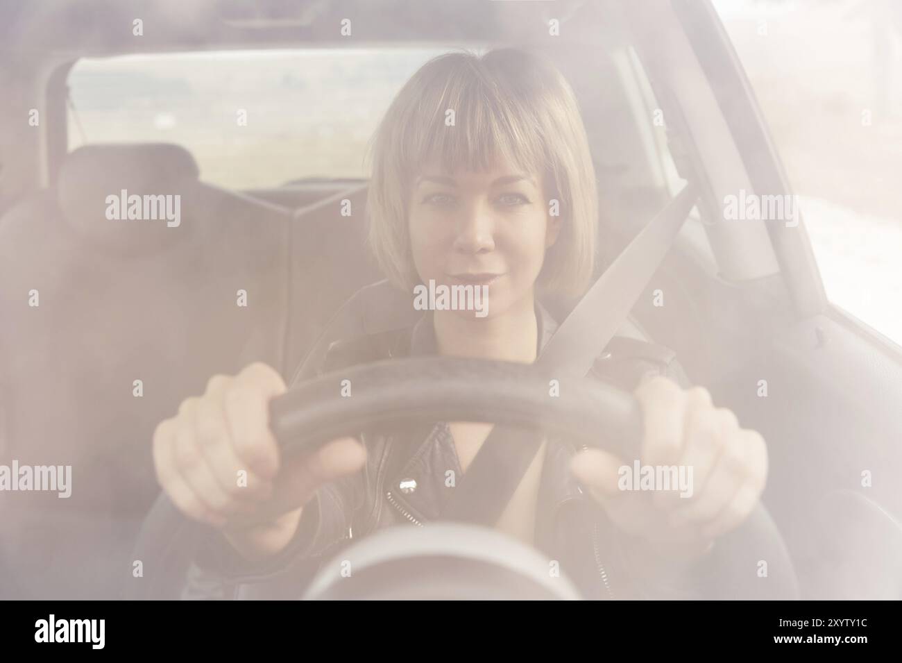 A cute young woman with a short haircut sits behind the wheel of a ...