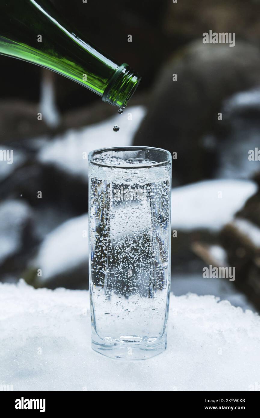 Pure mineral water is poured from a glass green bottle into a clear glass beaker until the last ...
