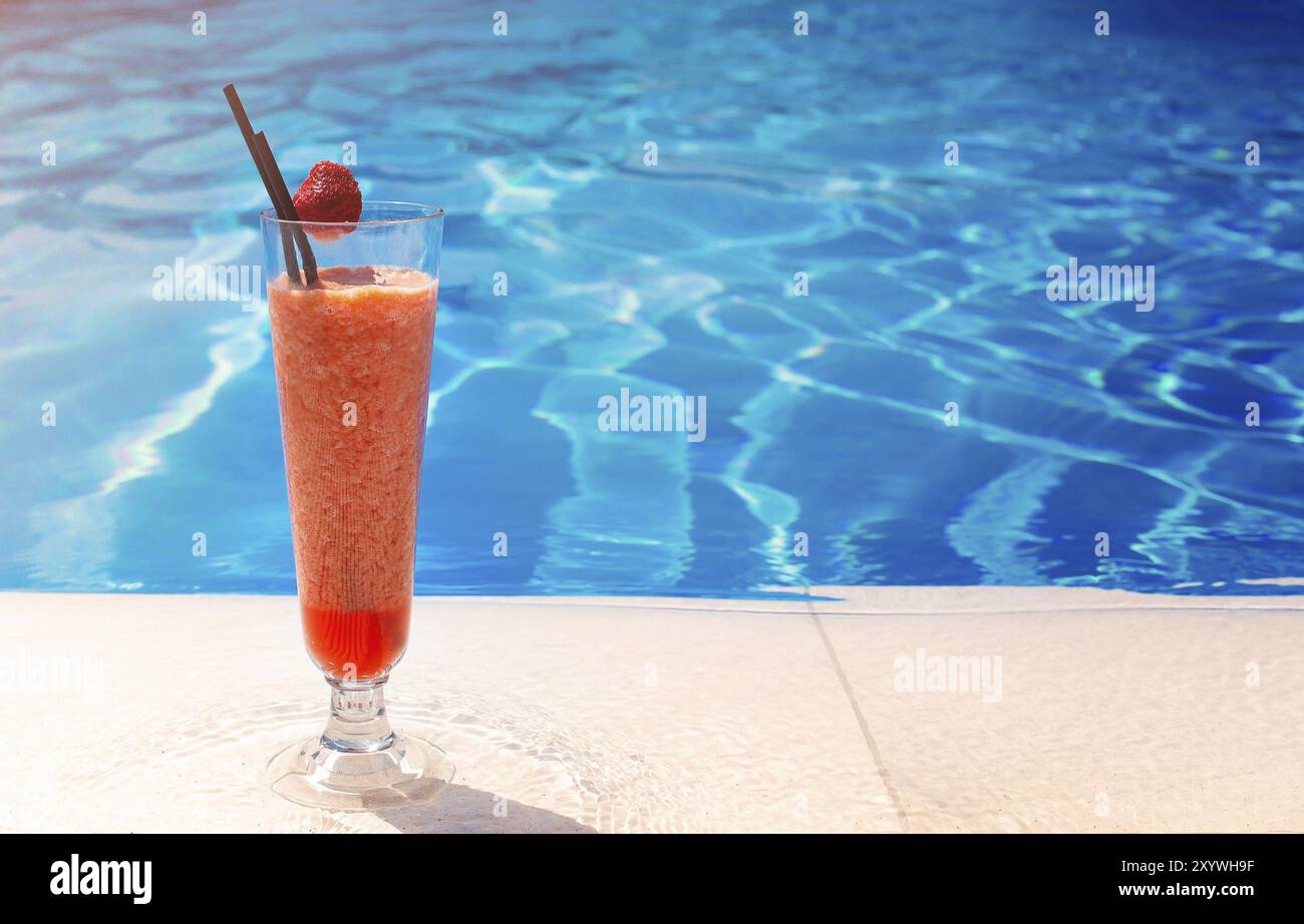 Glass with a bright red cocktail on the table by the pool. Luxury ...