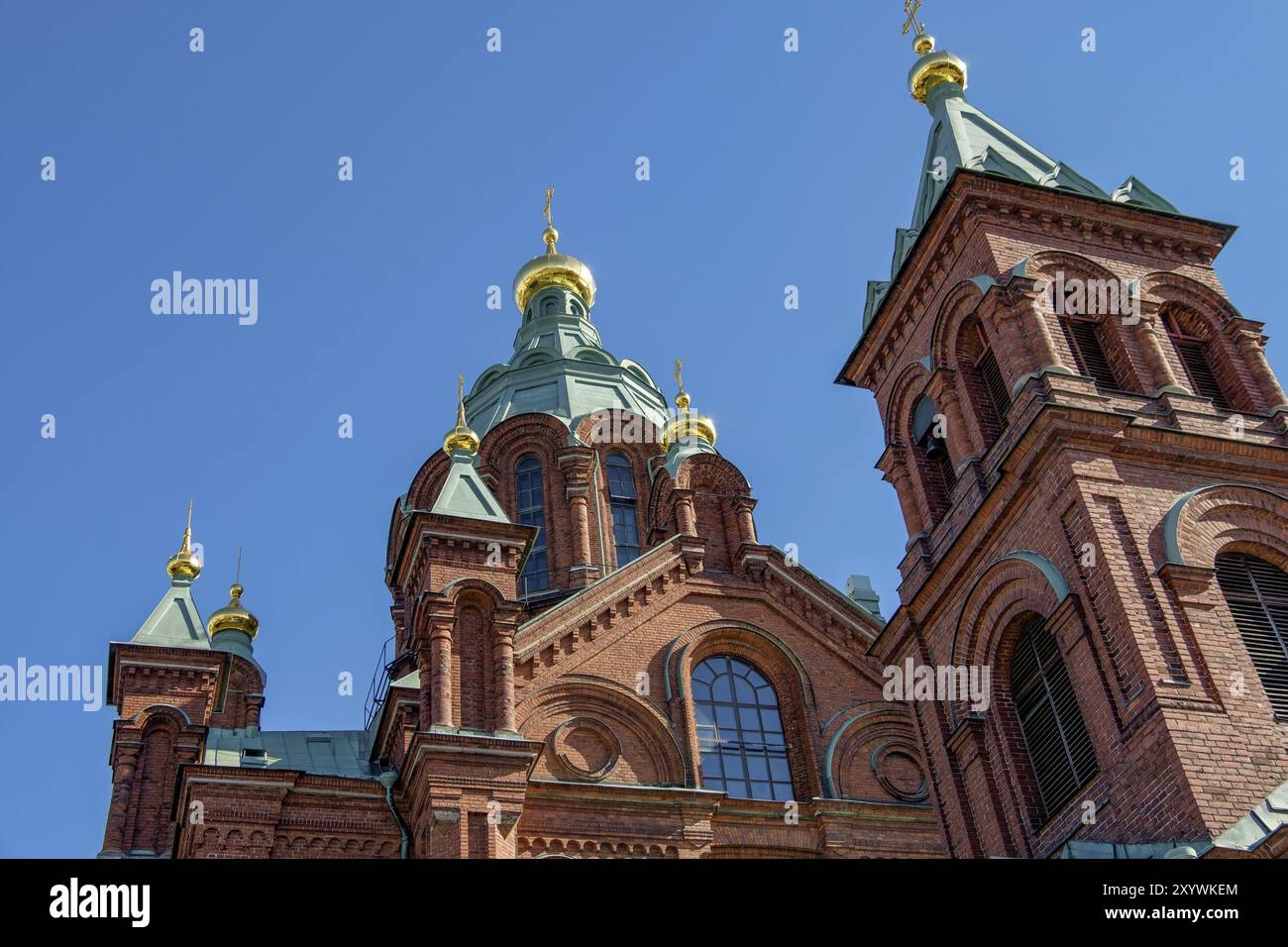 Brick church tower with green and golden domes under a clear blue sky ...