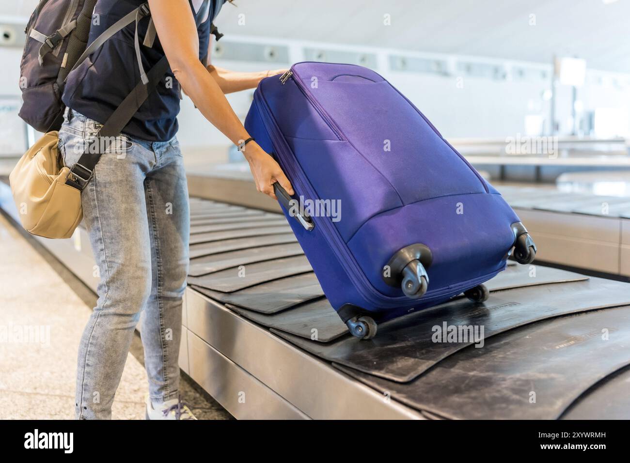A woman is pulling her blue suitcase off the conveyor belt at an ...