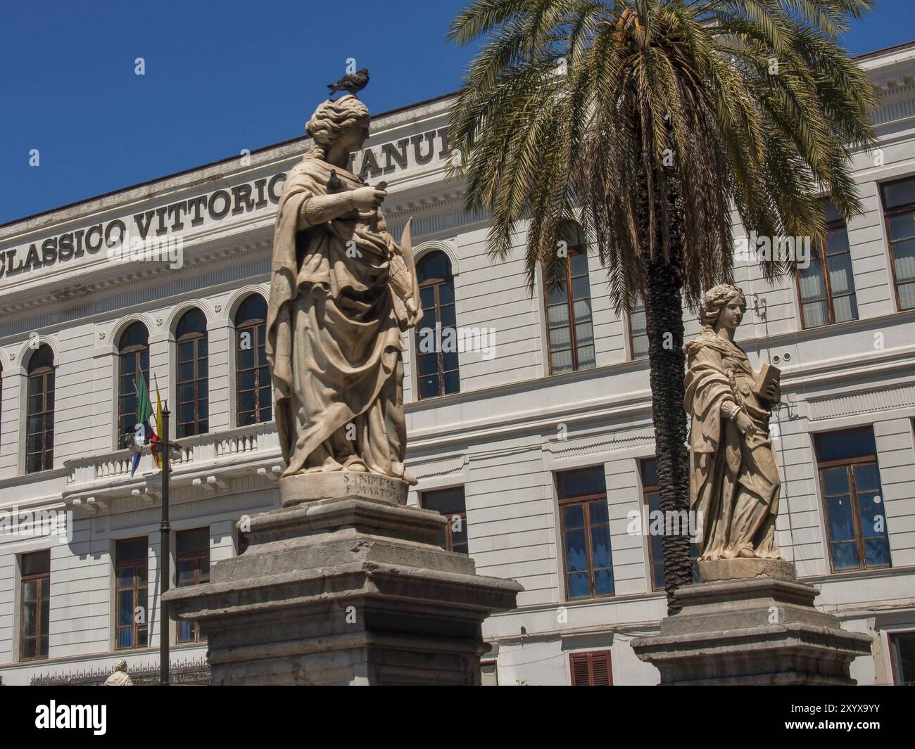 Two statues in front of a school building with a palm tree in classical ...