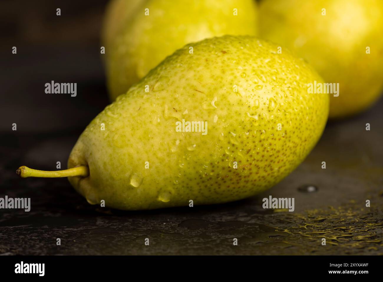 a green ripe pear covered with drops of water on the dark table, wet ...