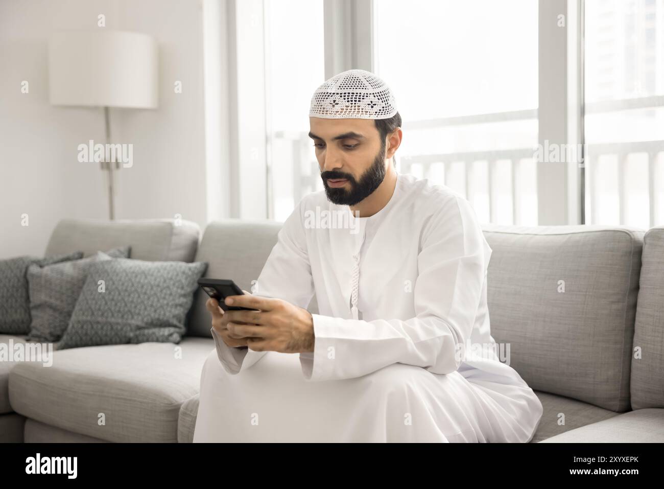 Serious handsome Arabic man in white Muslim clothes using application ...
