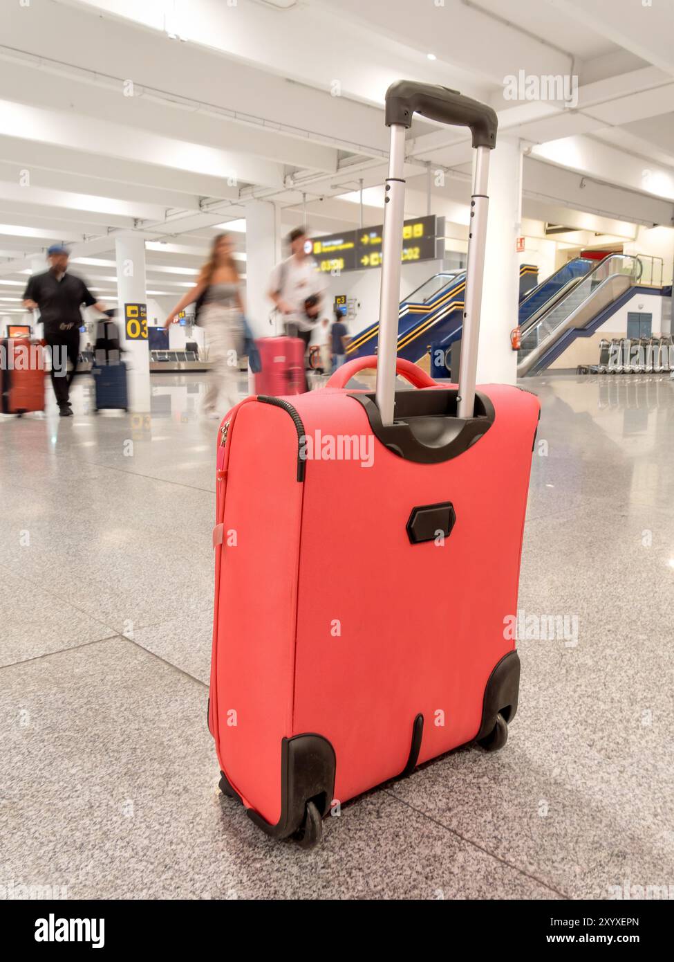 Red suitcase in busy airport terminal Stock Photo - Alamy