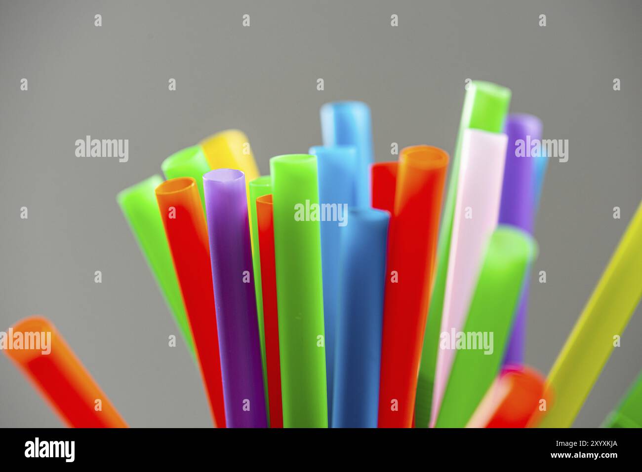 Multi colored plastic straws in a jar in front of a grey background ...