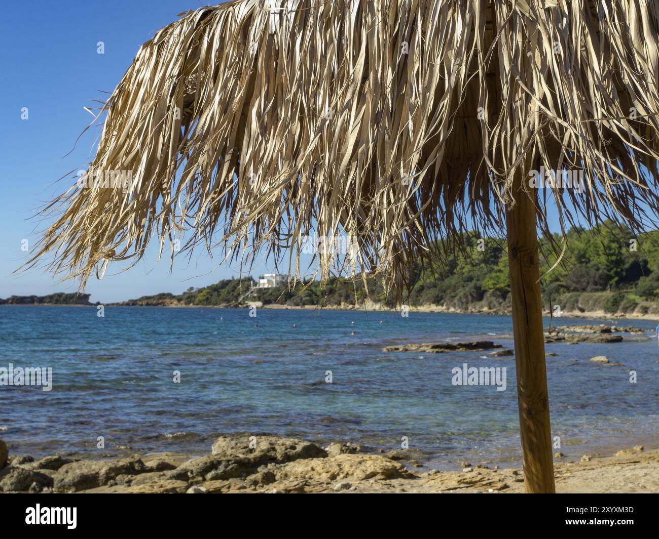 Thatched roof on a sandy beach, rocky coast and the blue sea under a ...