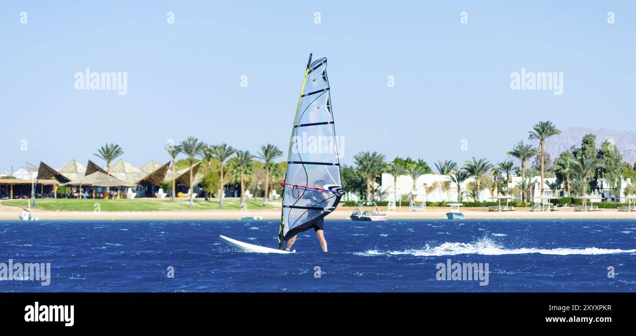 Windsurfer rides on the background of the beach with a hotel and palm ...