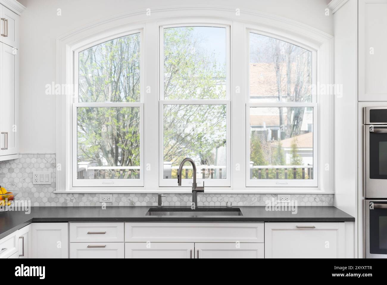 A kitchen detail with large arched windows, white cabinets, a dark grey ...