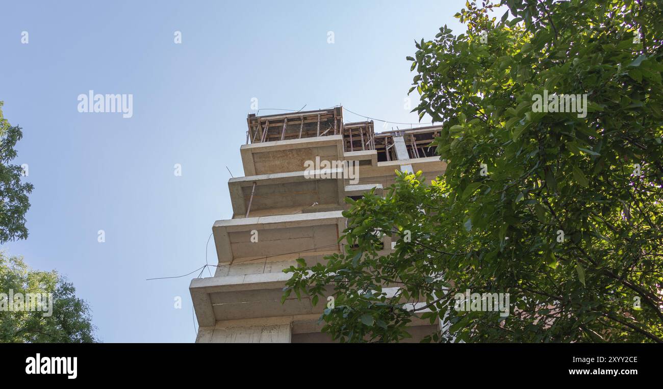 A tall building with white concrete slabs. The top floors are under ...