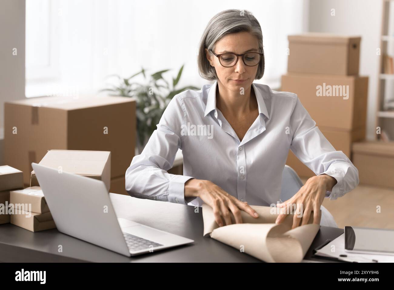 Serious mature woman wrapping parcel with paper Stock Photo - Alamy