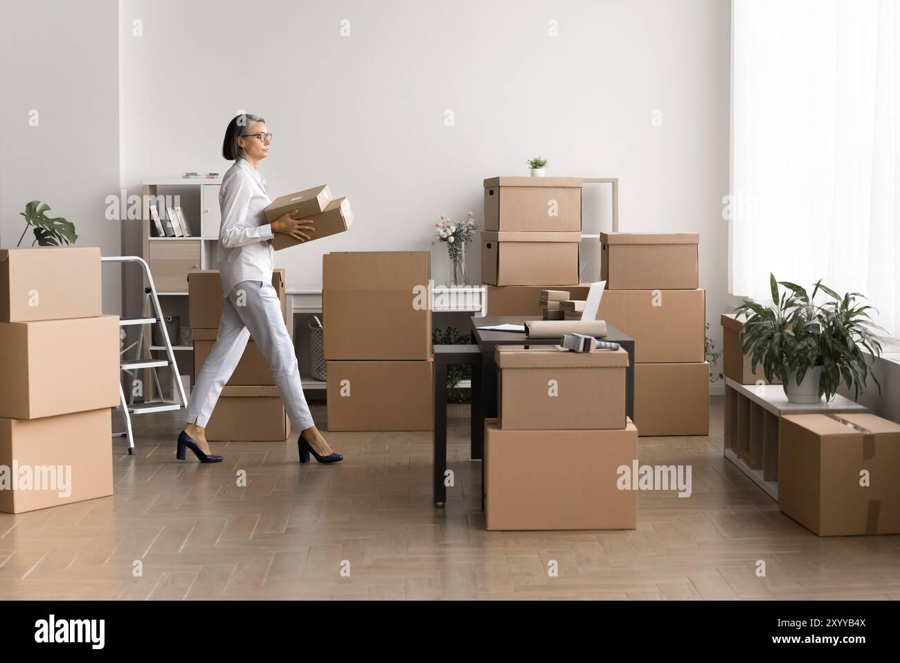 Woman carrying cardboard boxes in room filled with stacked parcels ...