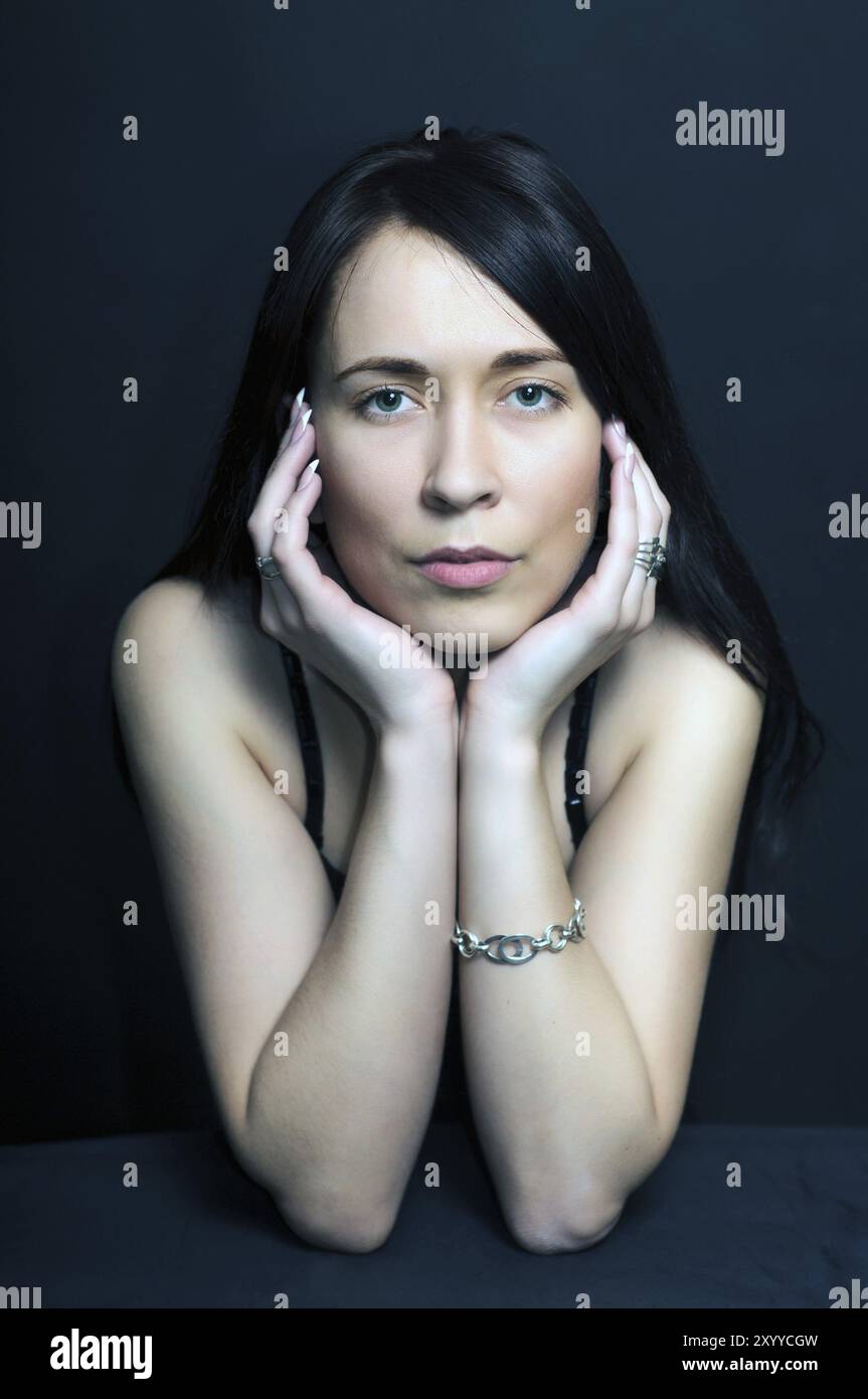Portrait Of A Young Brunette Woman With Arms Crossed Under Her Chin On Dark Black Background