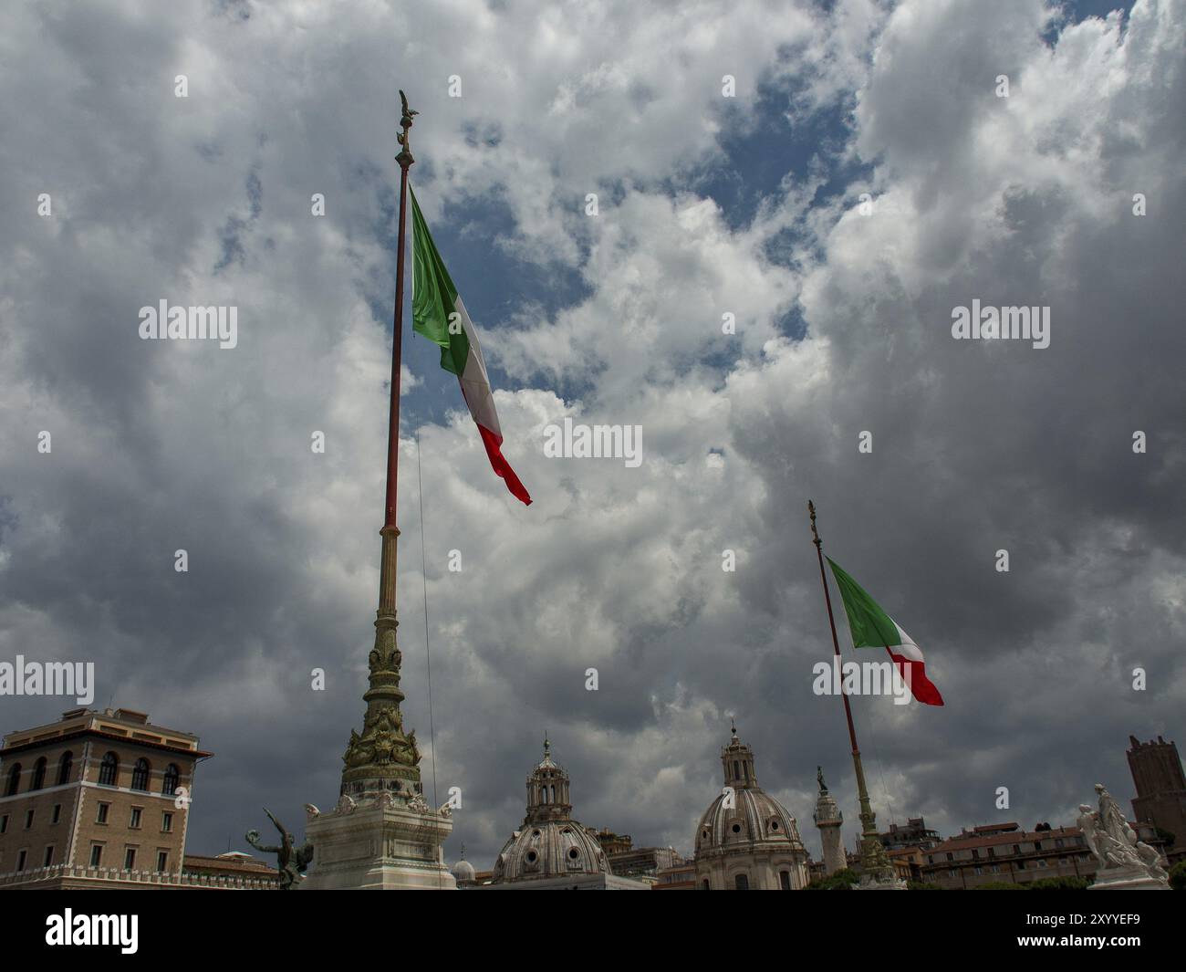 Two Italian flags waving under a cloudy sky in front of historic ...