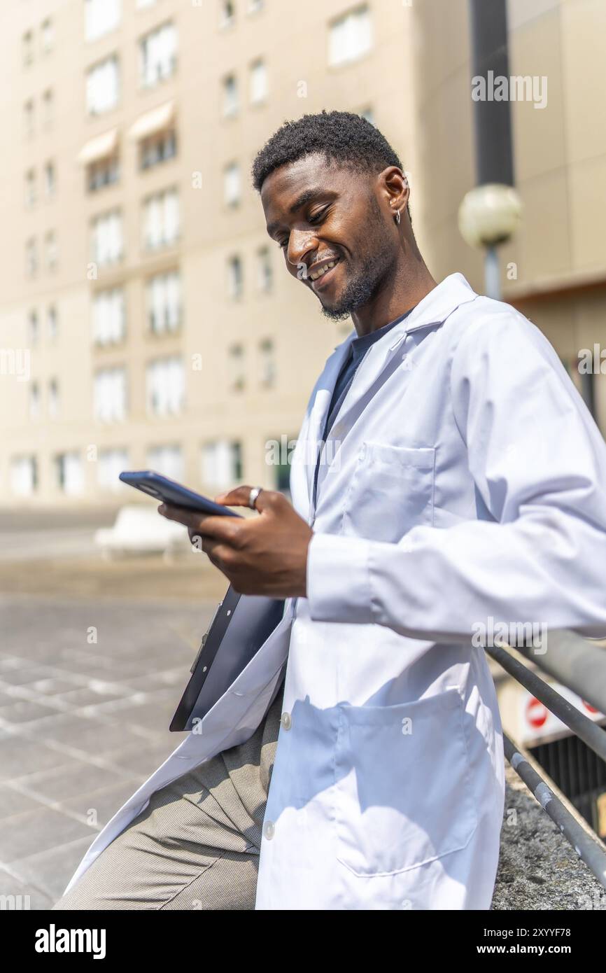 Vertical photo of a cheerful young african doctor using phone during ...