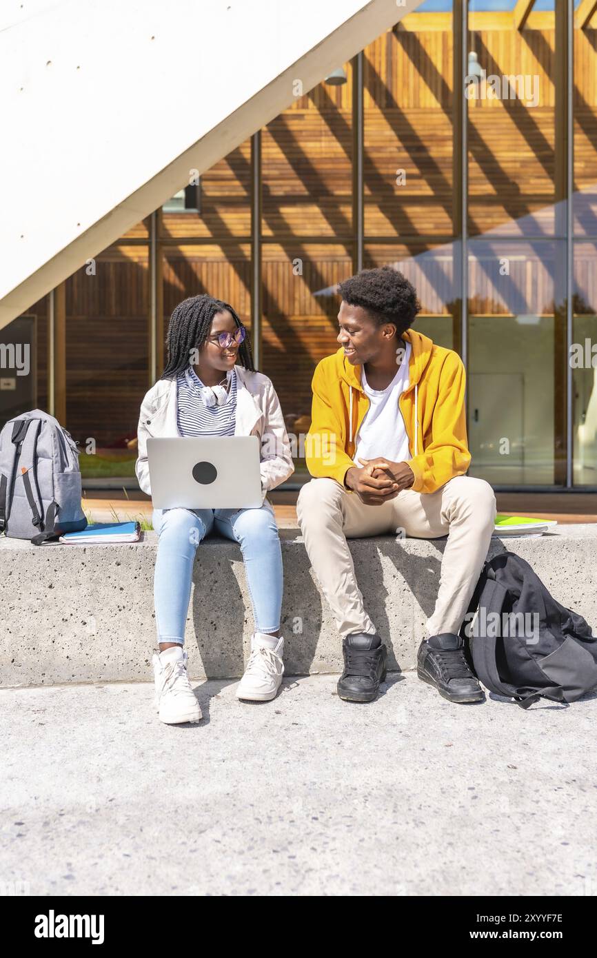 Vertical photo of two african students using laptop sitting outside the ...