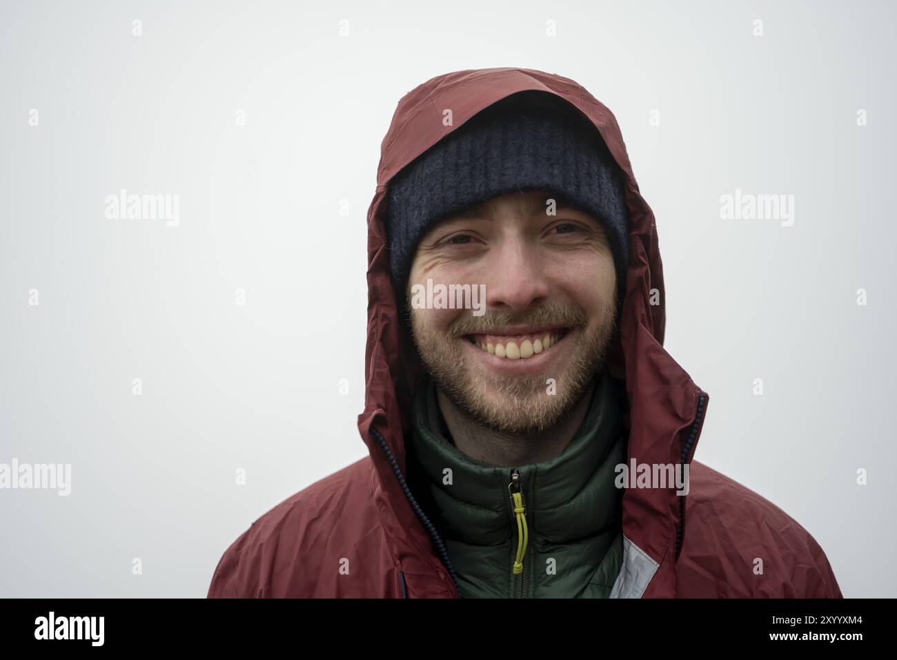 Young man with cap and rain jacket in foggy weather, smiling, portrait ...