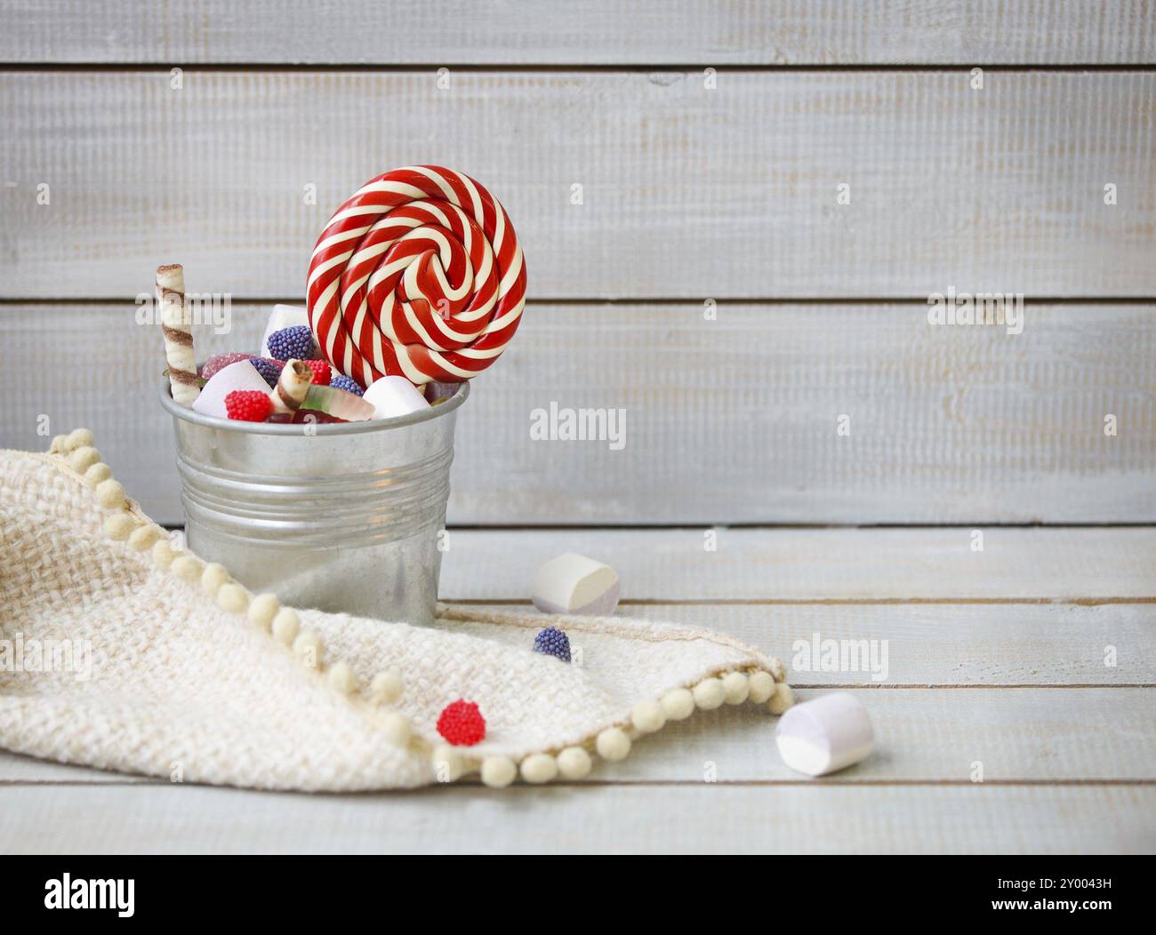 Colorful candies in a small bucket on light wooden background with copy ...