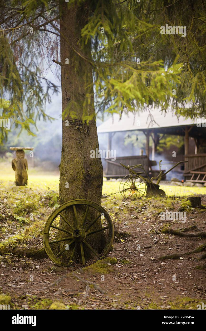 An old wagon wheel on a tree trunk in front of a hut made of wood smoke ...
