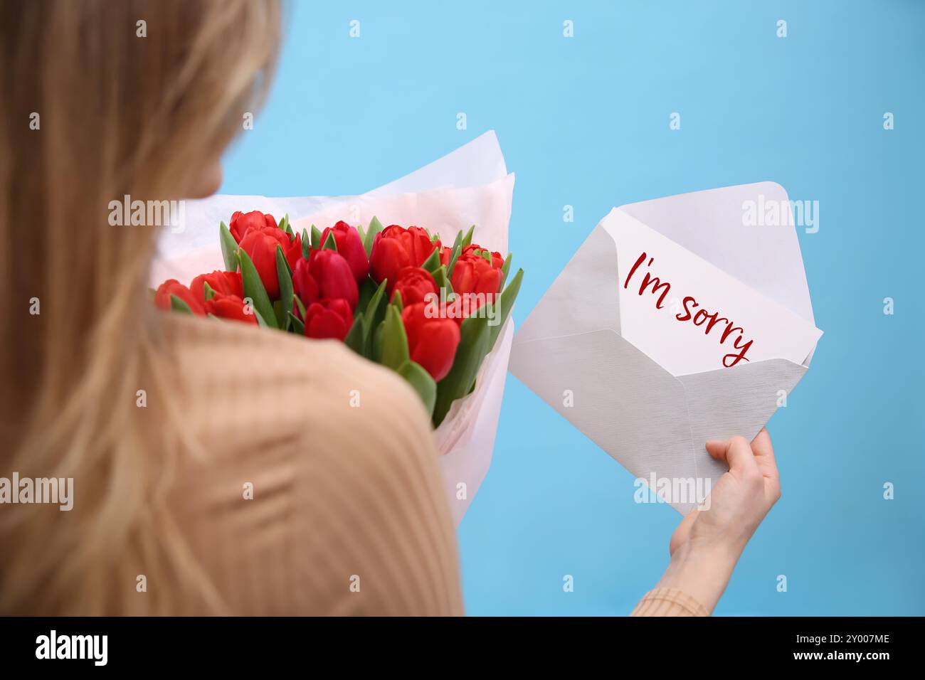Woman with sorry card and bouquet of flowers on light blue background ...