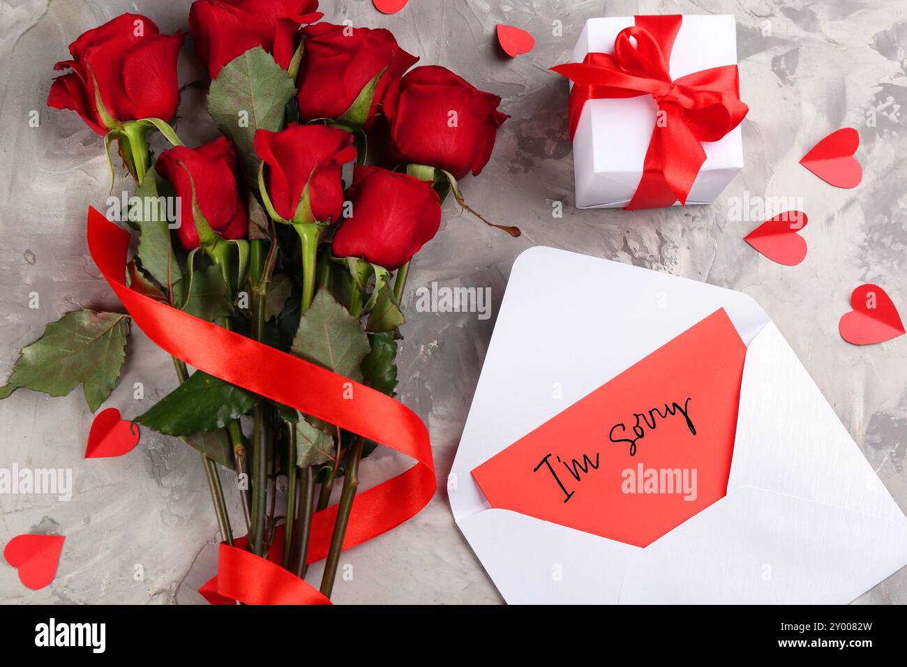 Sorry card in envelope, gift box and red roses on grey table, top view ...